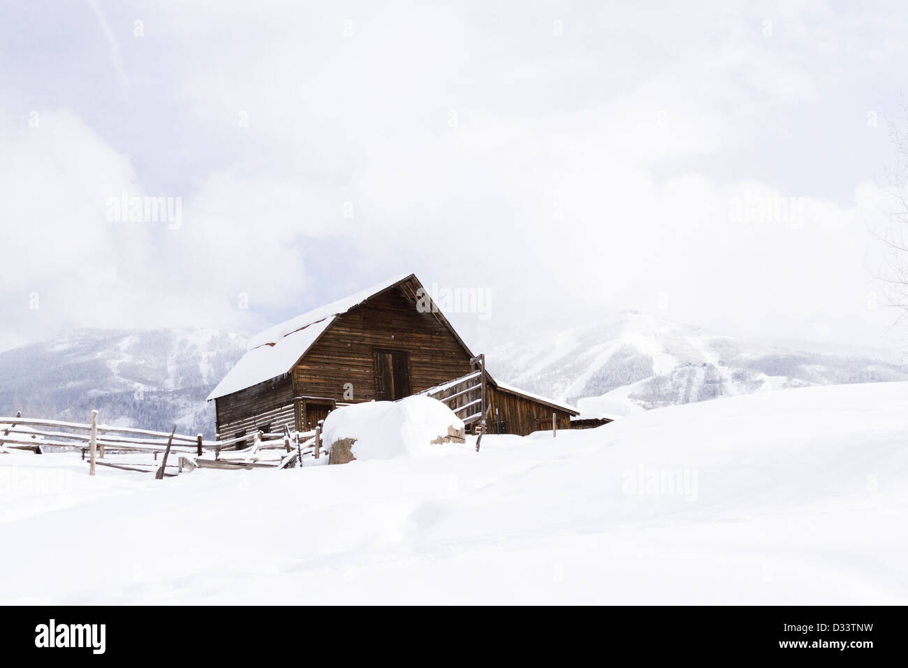 Aged barn on snowy hillside with ski lifts and ski slopes in background ...