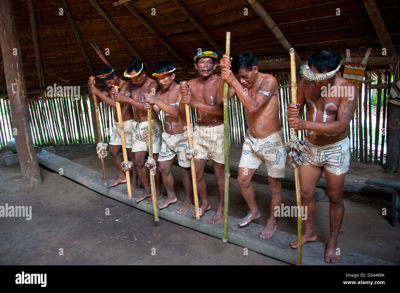 A group of Bora men singing and dancing with poles inside a maloca ...