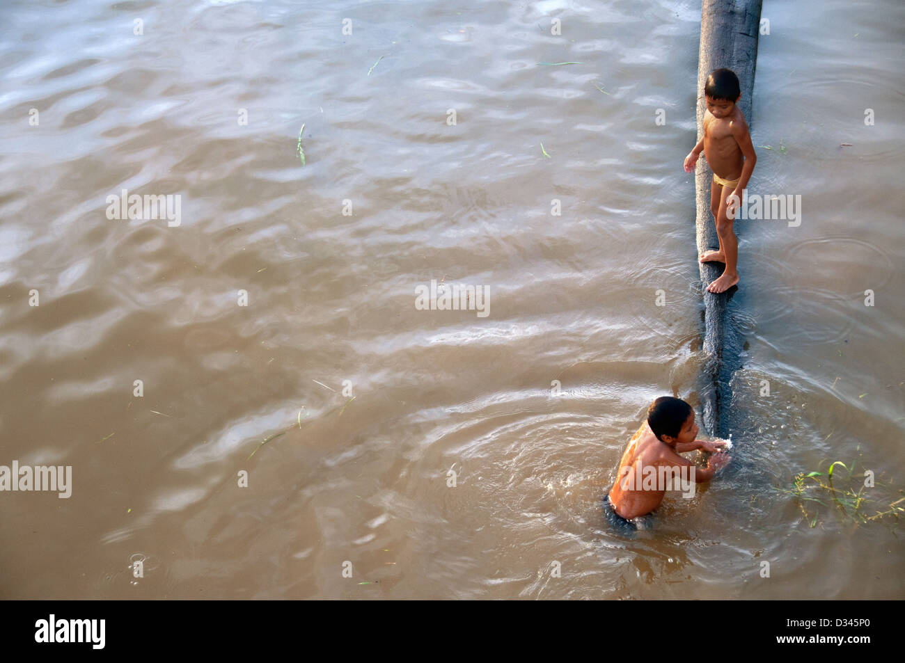 Two children playing on a trunk in the water, Pebas, Amazonian Peru ...