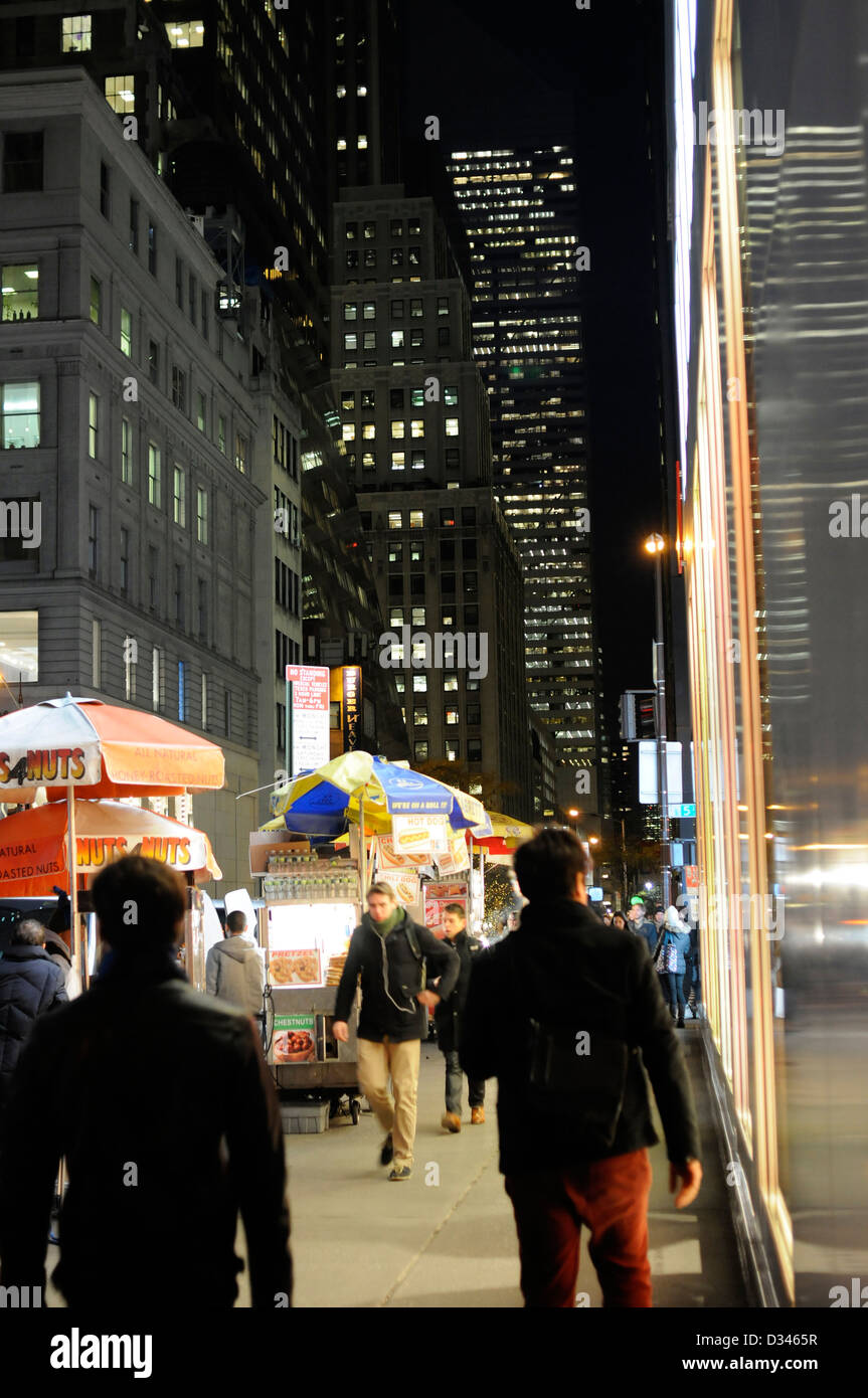 Tourists, pedestrians and shoppers on a busy street corner at night ...