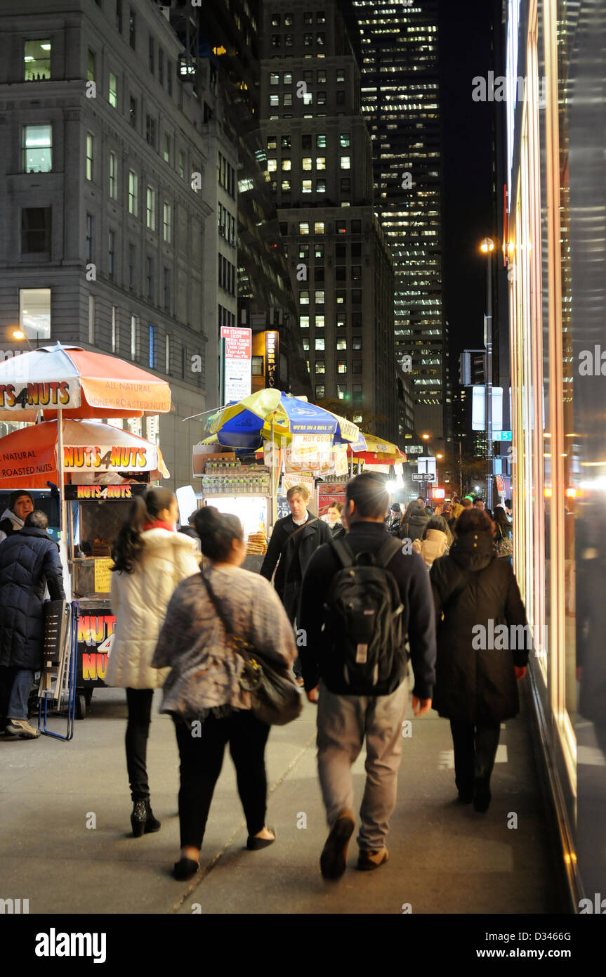 Tourists, pedestrians and shoppers on a busy street corner at night ...
