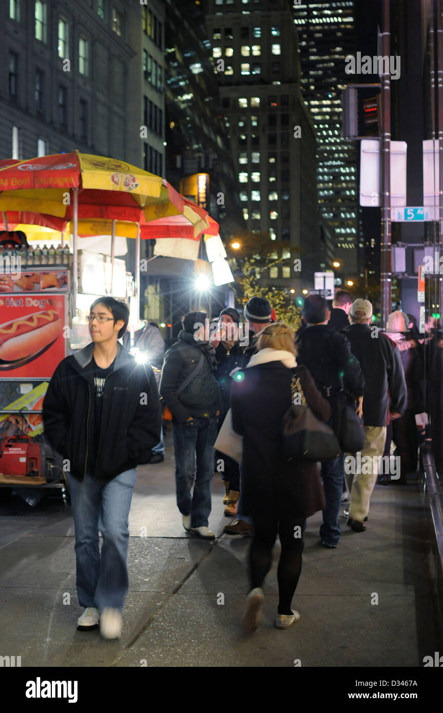 Tourists, pedestrians and shoppers on a busy street corner at night ...