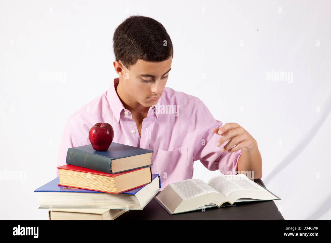A teenage student, sitting with a stack of books and looking seriously ...