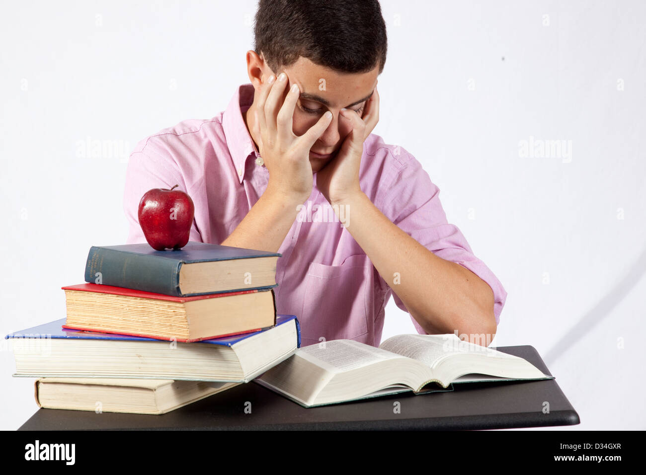 A teenage student, sitting with a stack of books and looking seriously ...