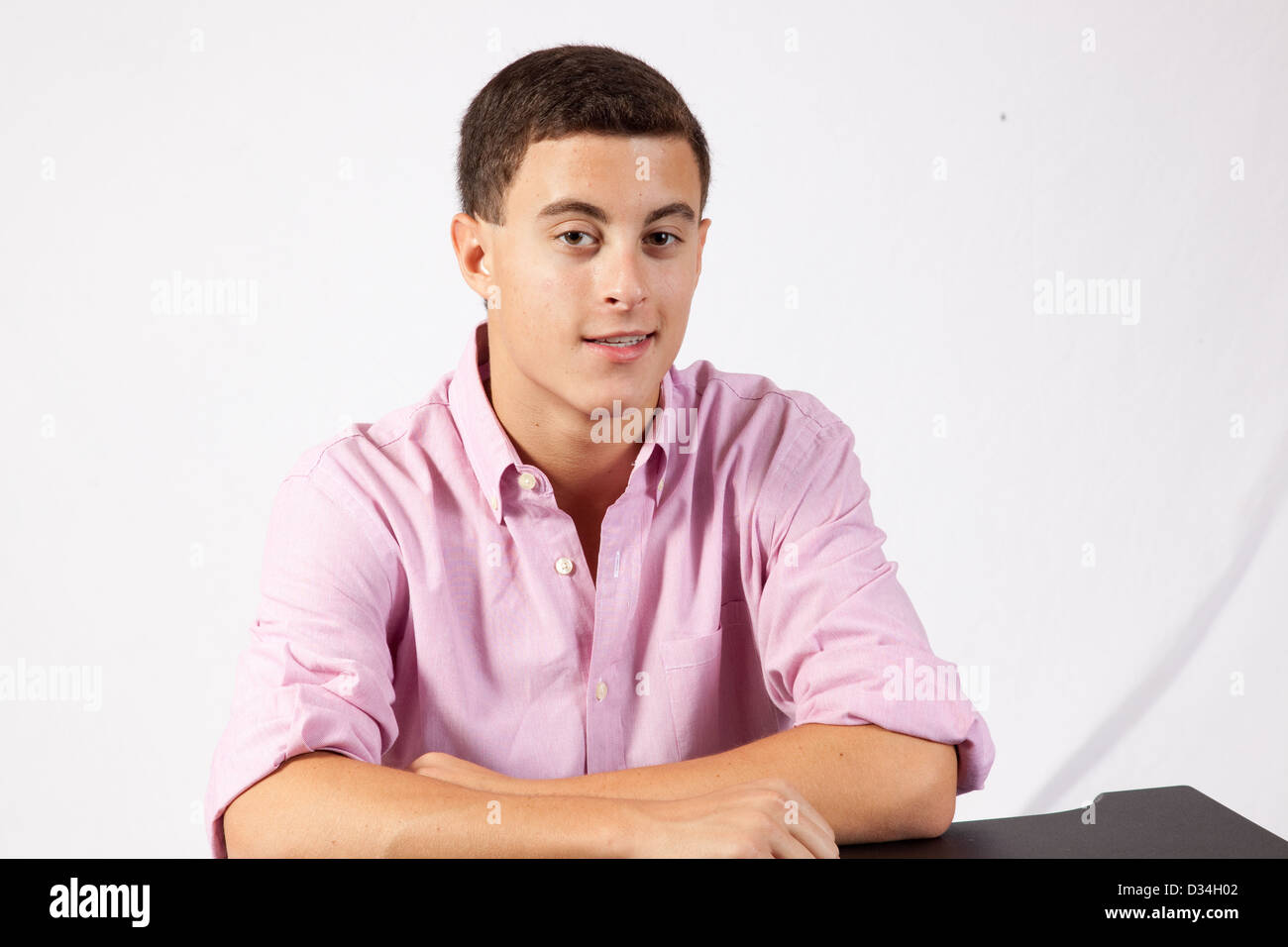 Handsome teenage boy, sitting at a table with his arms propped on it ...