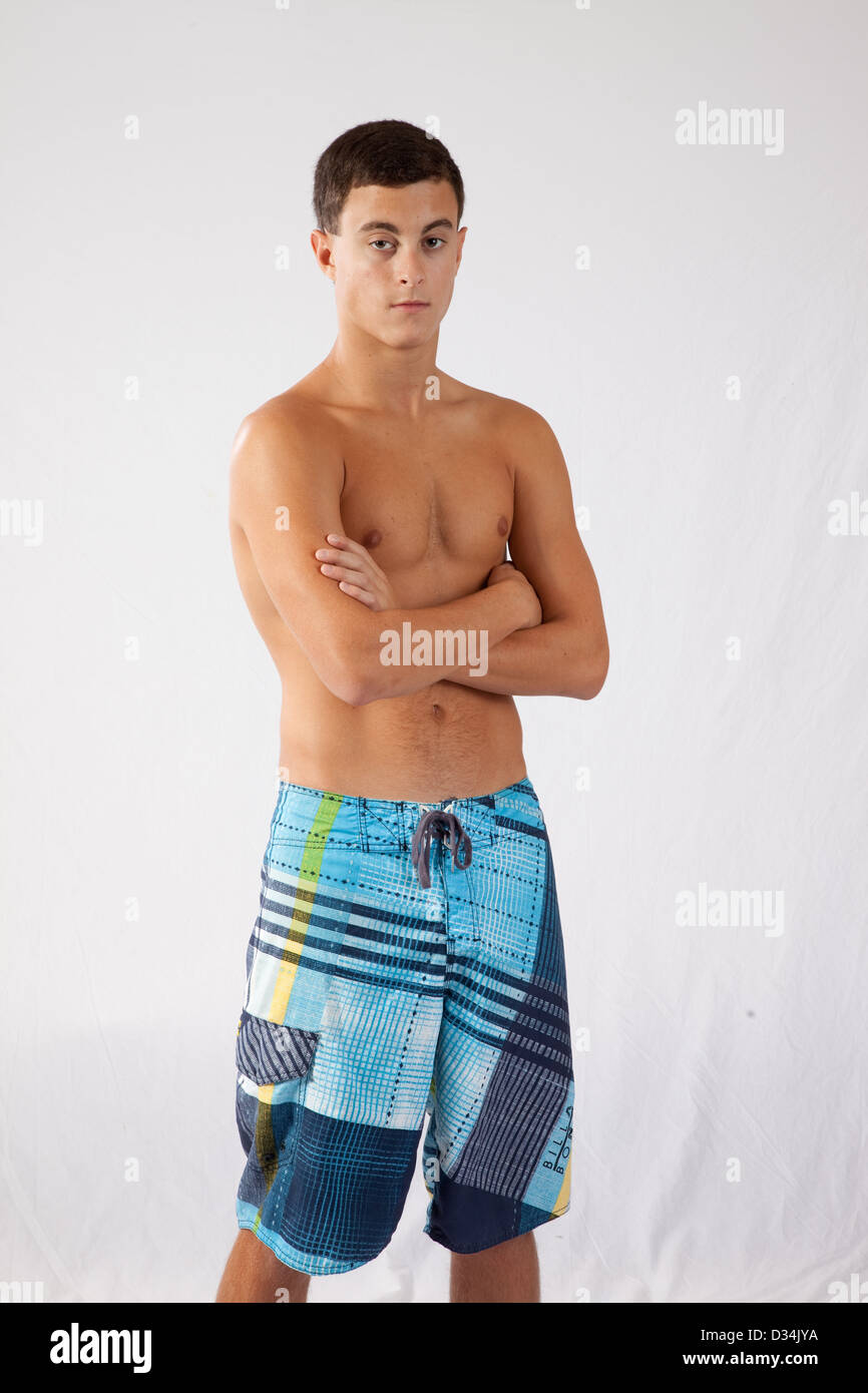 Teenage boy standing shirtless and in swim trunks, with his arms folded ...