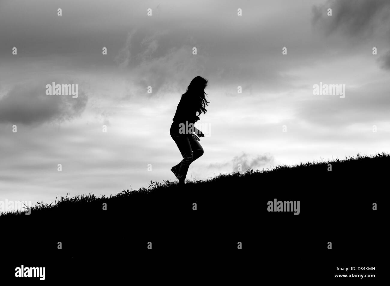 Silhouette of girl running up a grassy hill slope Stock Photo - Alamy