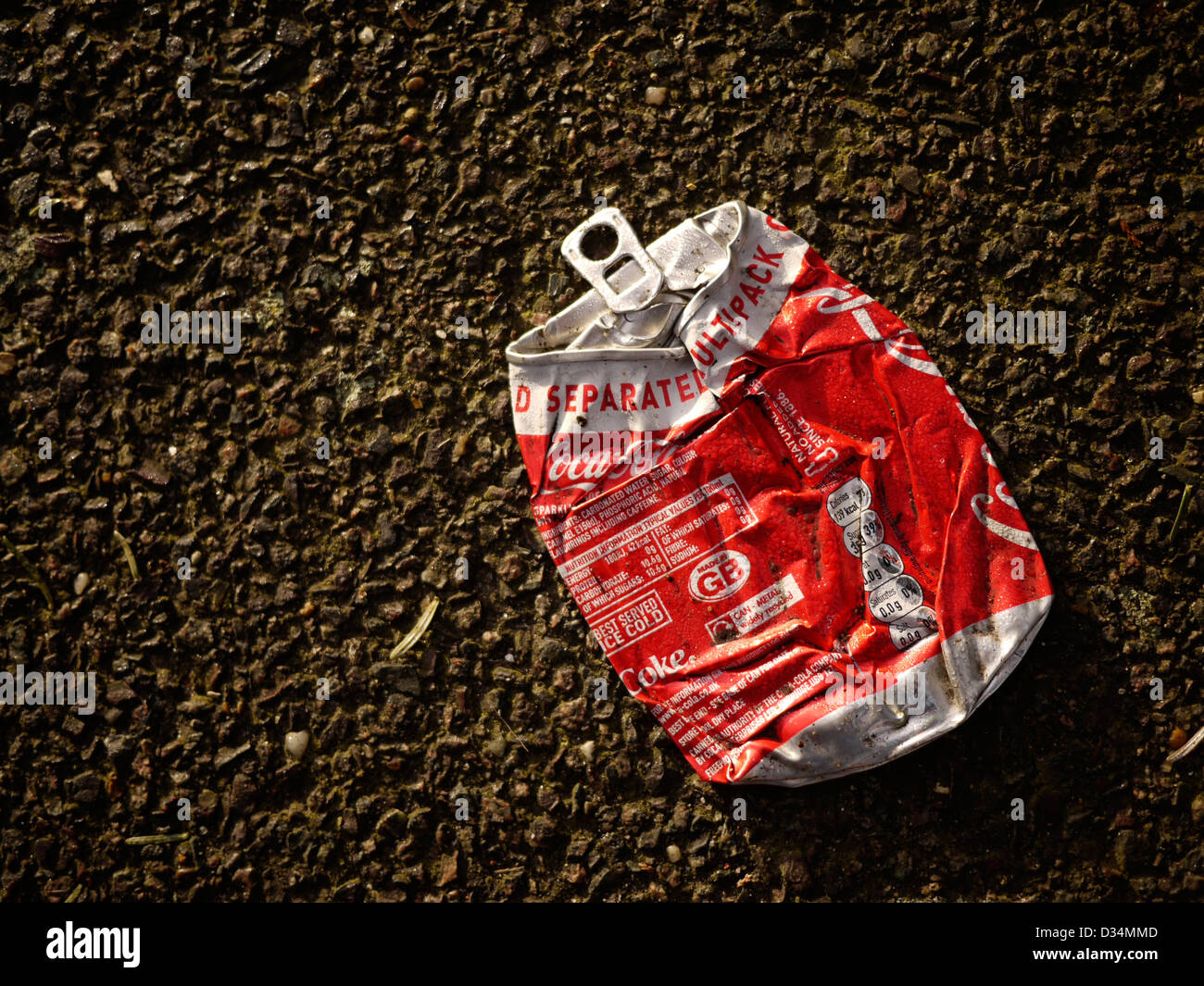 A crushed and discarded Coca-Cola can lies on a city street ...