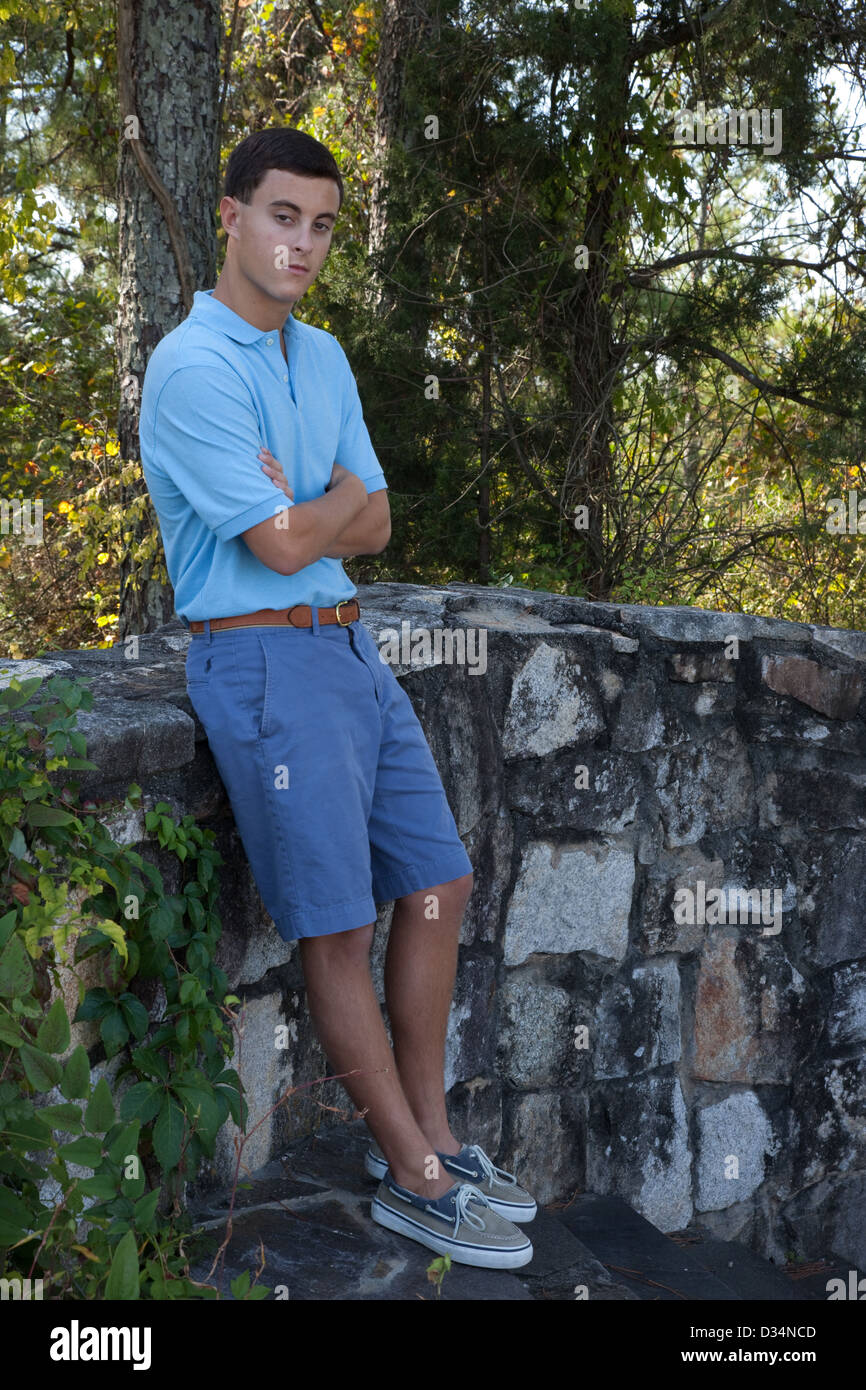 Handsome young man outside standing against a stone wall and looking at ...