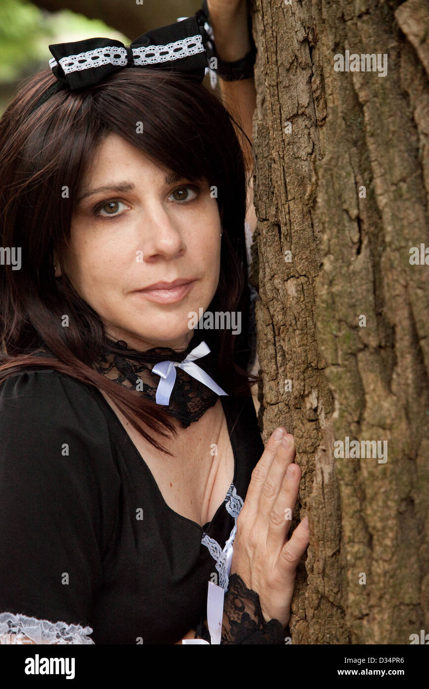 Cute white woman in a maid's outfit, standing outside against the rough ...