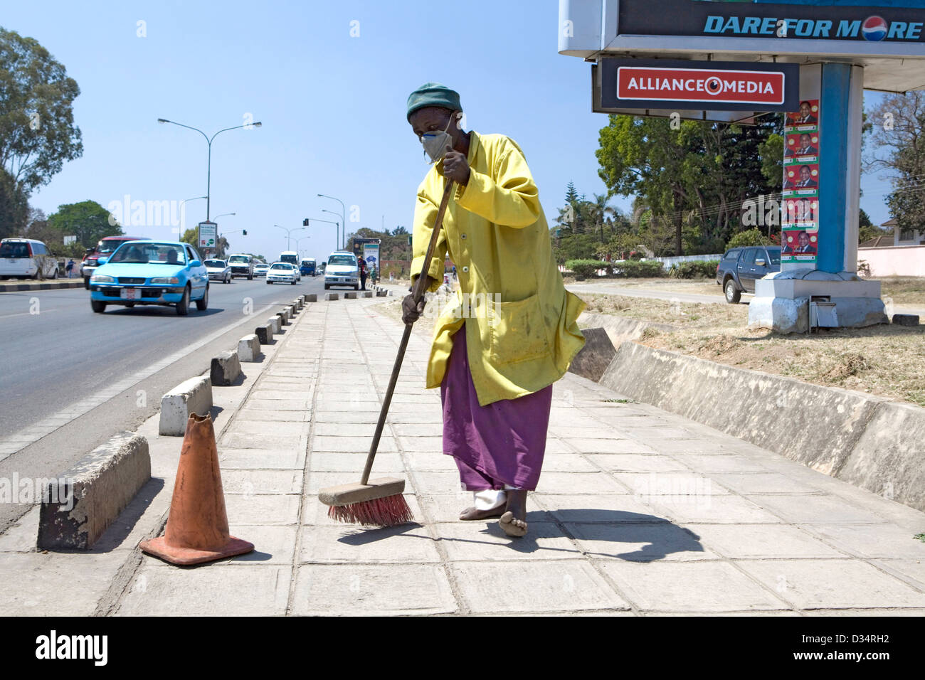 A Government employee sweeping the pavement on the side of a busy major ...