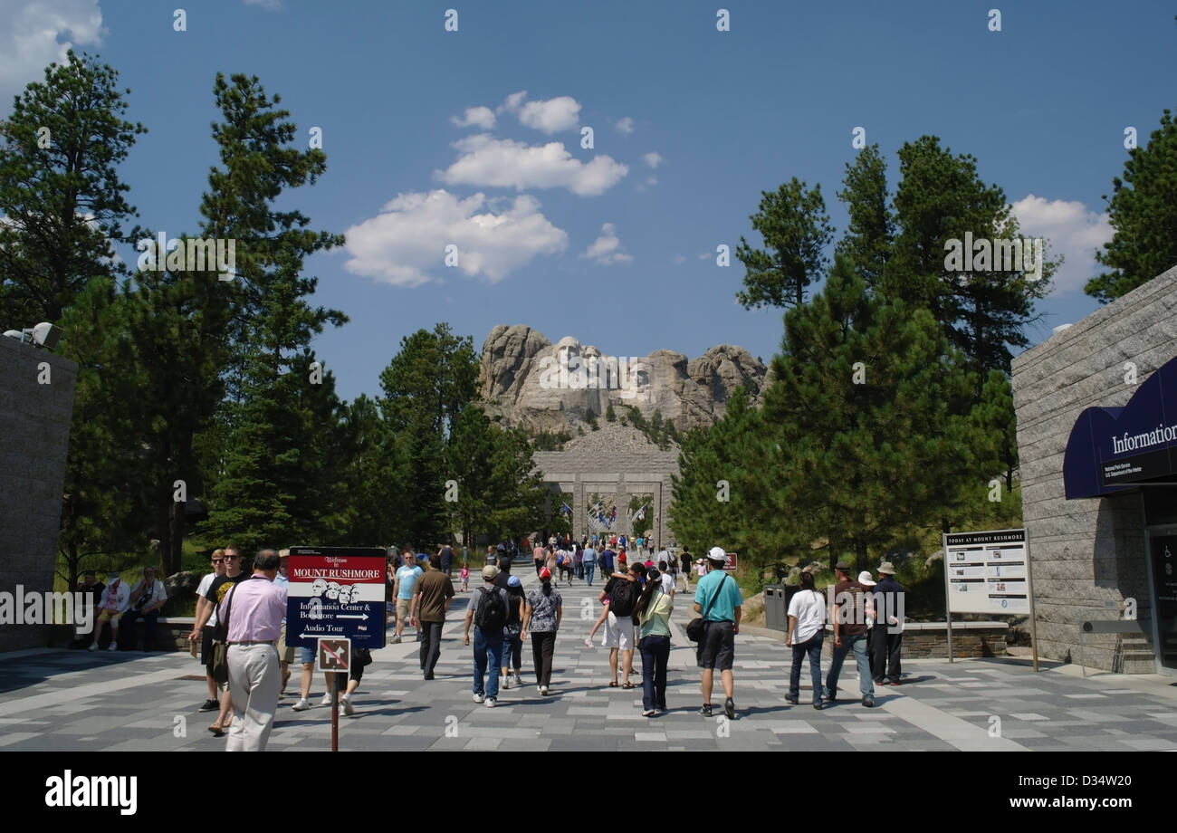People walking tree-lined entrance walkway towards cliff-face American ...