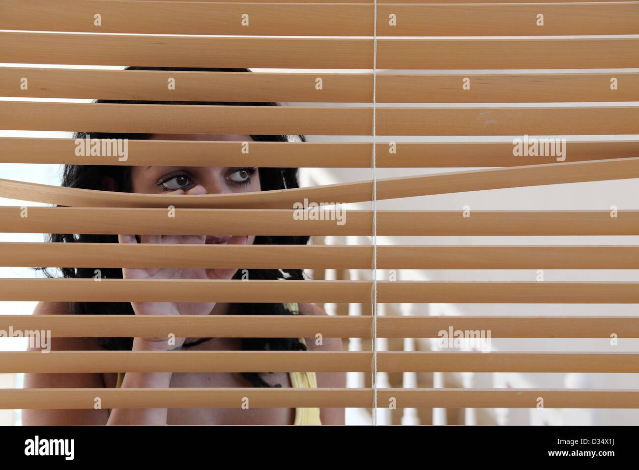 Young dark haired female behind a window blind, looking out of the ...