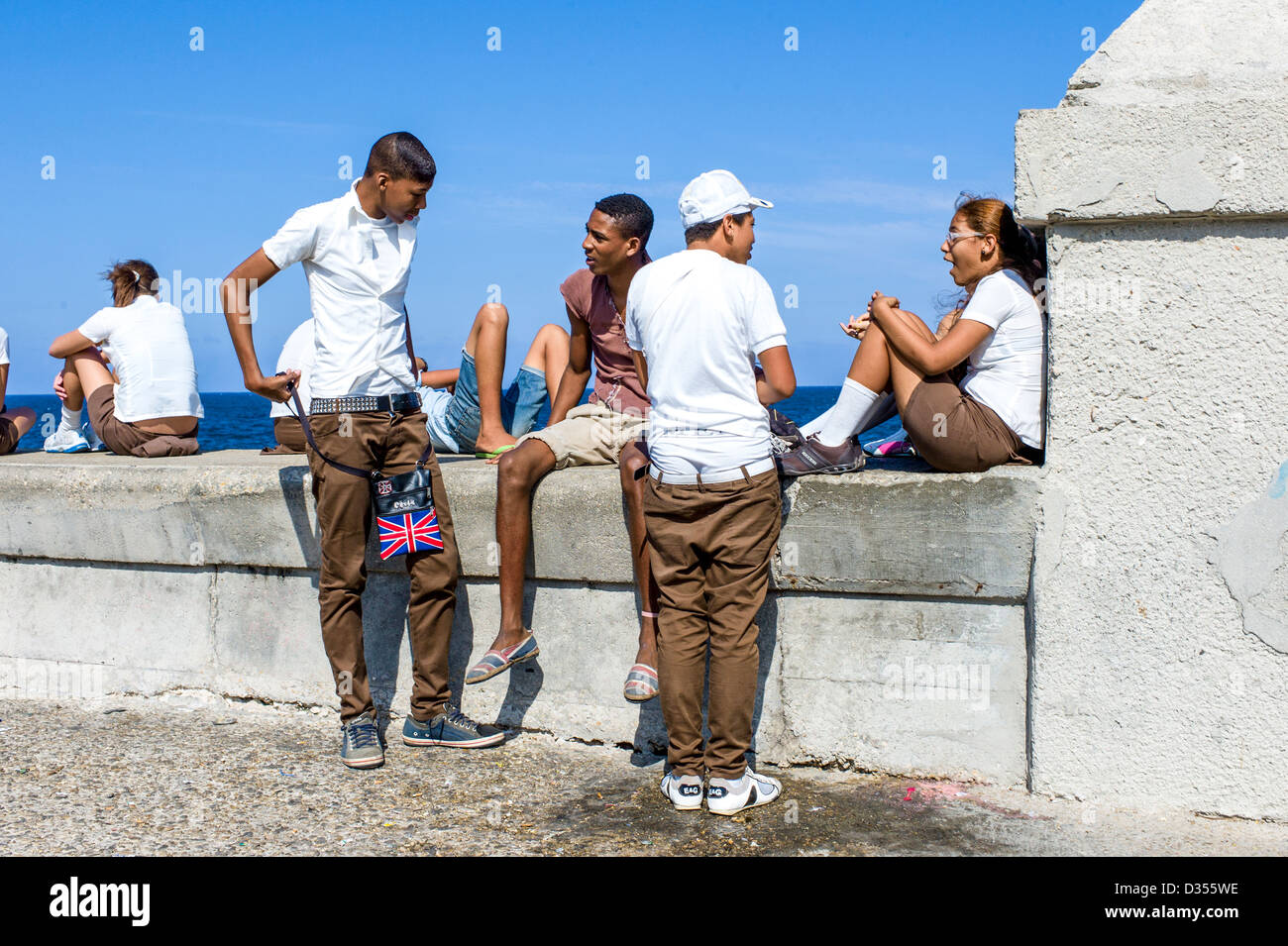 School children on a break sitting and standing around the sea wall at ...