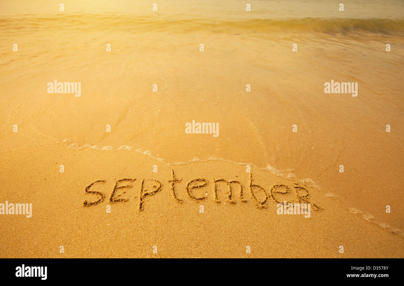 September - written in sand on beach texture - soft wave of the sea ...