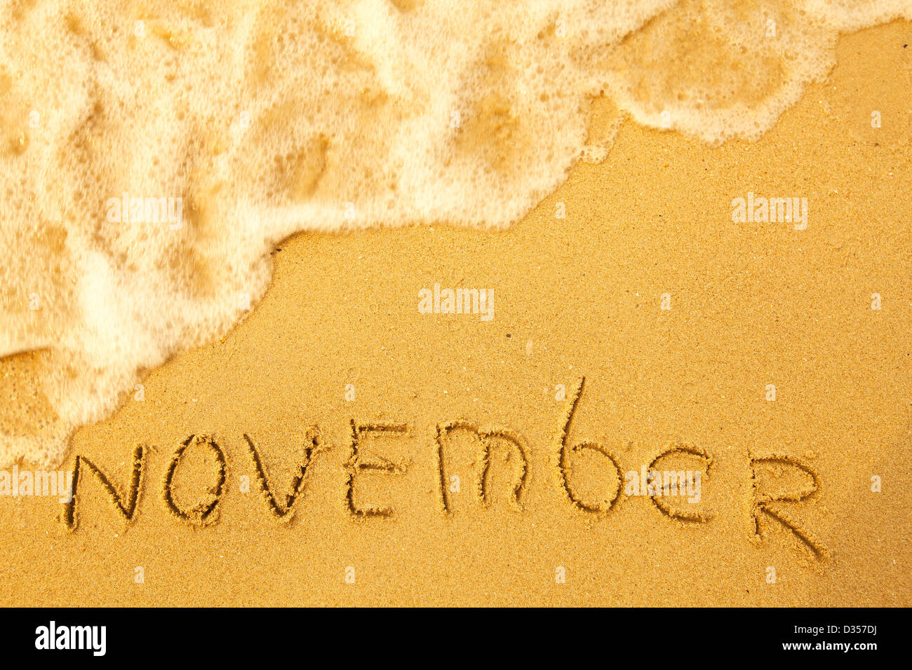 November - written in sand on beach texture - soft wave of the sea ...