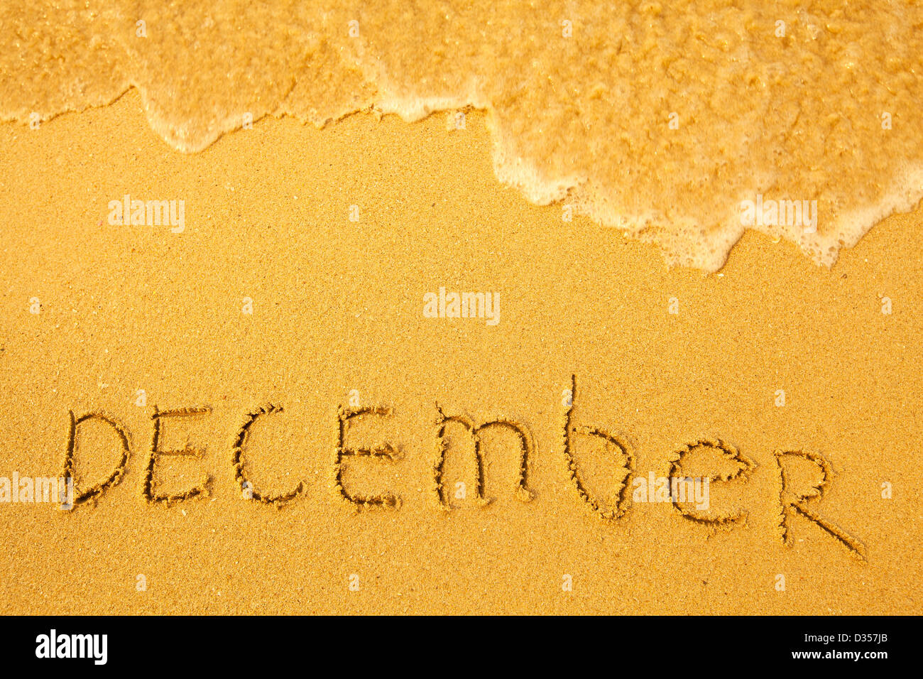 December - written in sand on beach texture - soft wave of the sea ...