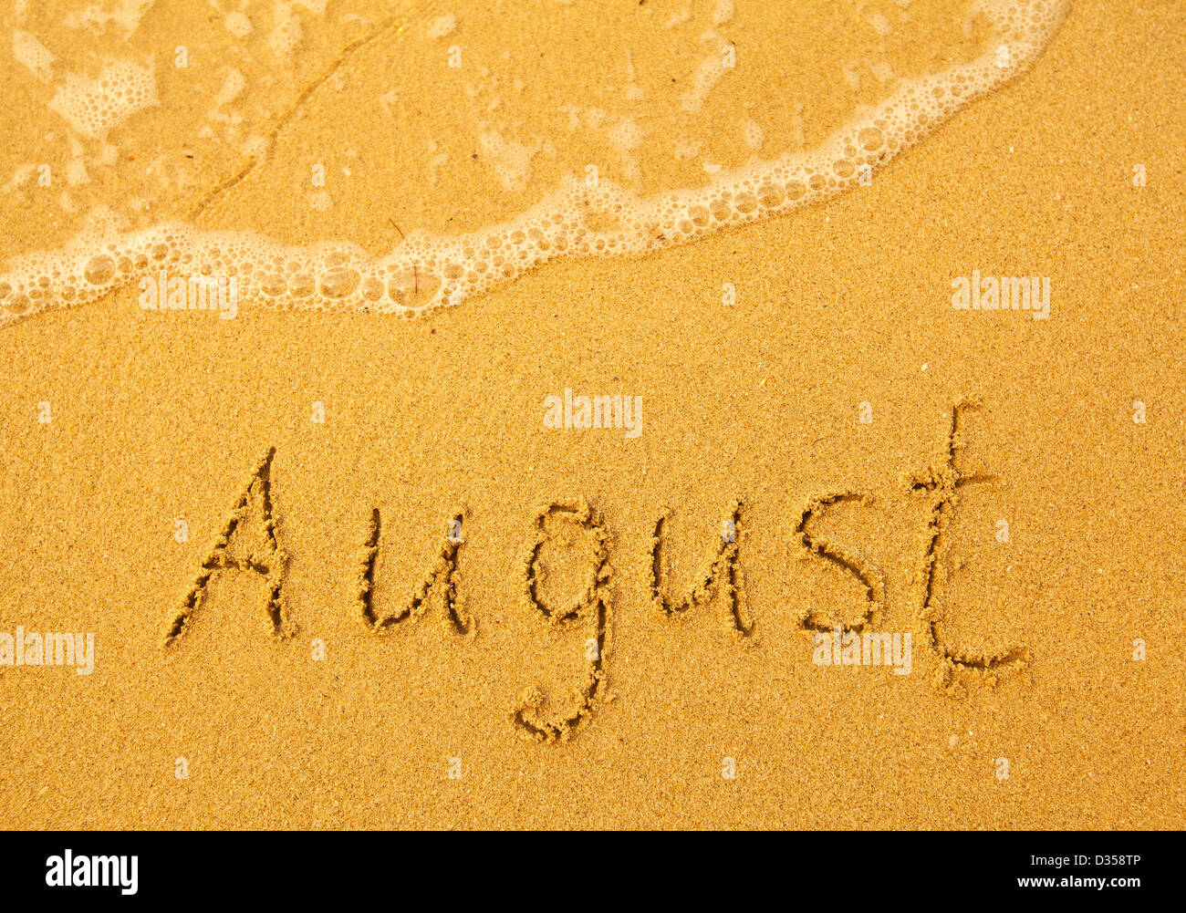 August - written in sand on beach texture - soft wave of the sea ...