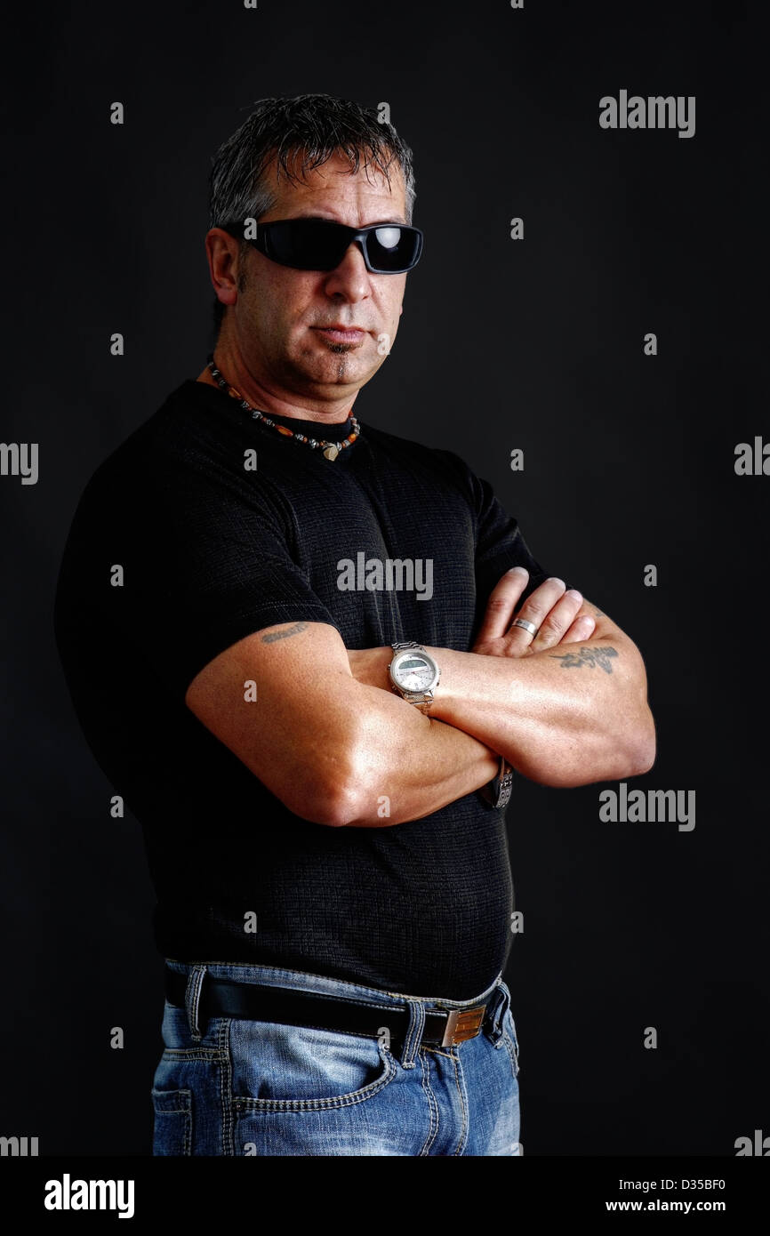 Somber tough guy with tatoos and black sunglasses, arms crossed ...