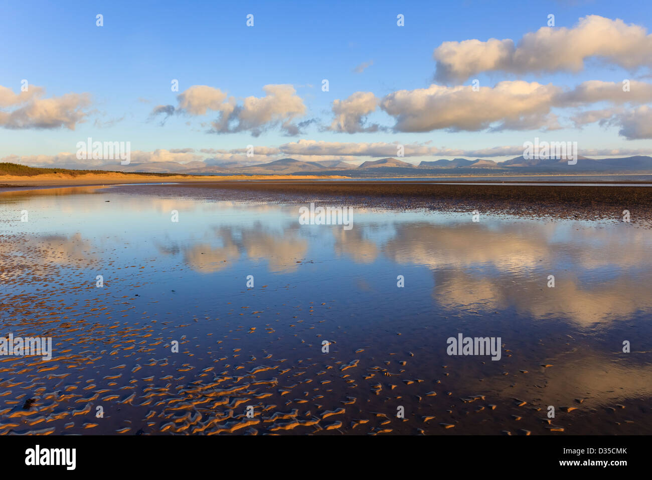Tidal pool reflecting clouds on Traeth Llanddwyn beach and bay at low ...