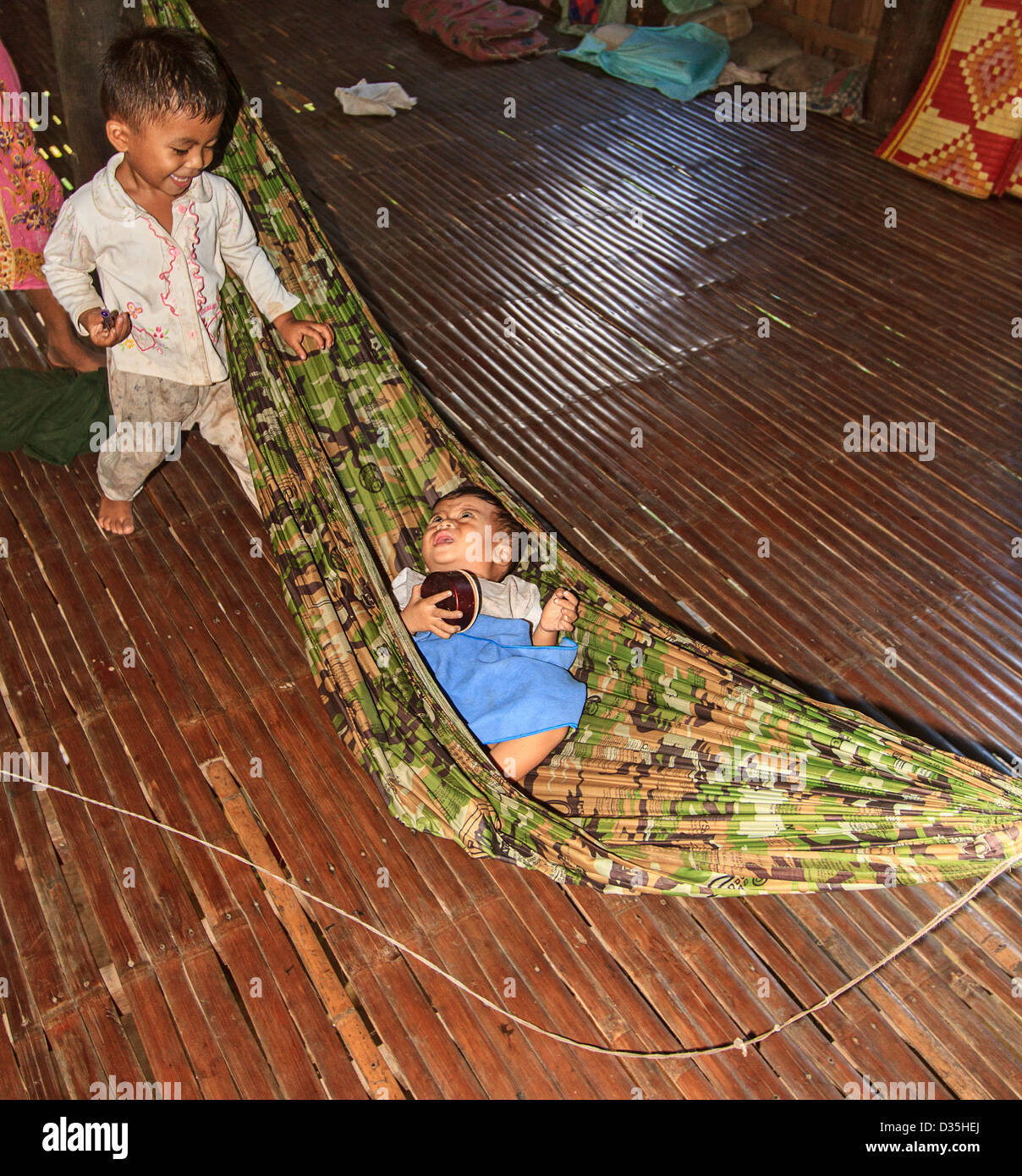 Young boy rocks his baby sister in hammock in their house on Koh Trong ...