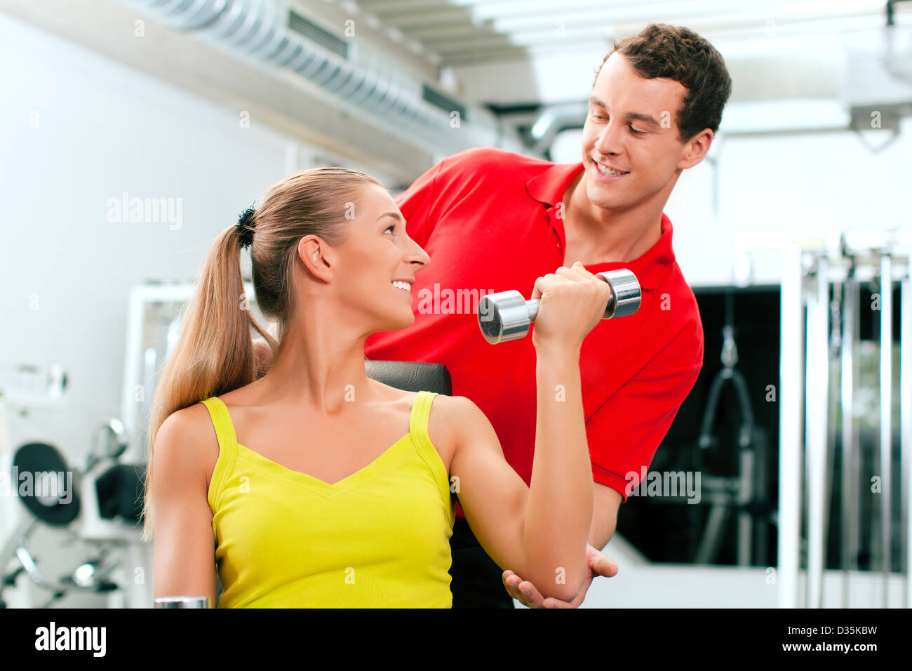 Young woman lifting a dumbbell in the gym assisted by her personal ...