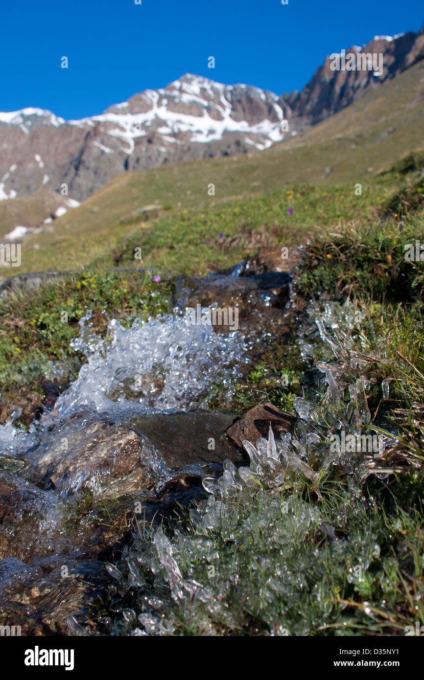 Frozen water and icicles in alpine stream with background of a snow ...