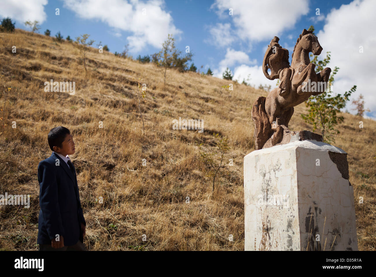 A Kyrgyz schoolboy looks on at a statue of Manas in the resettlement ...