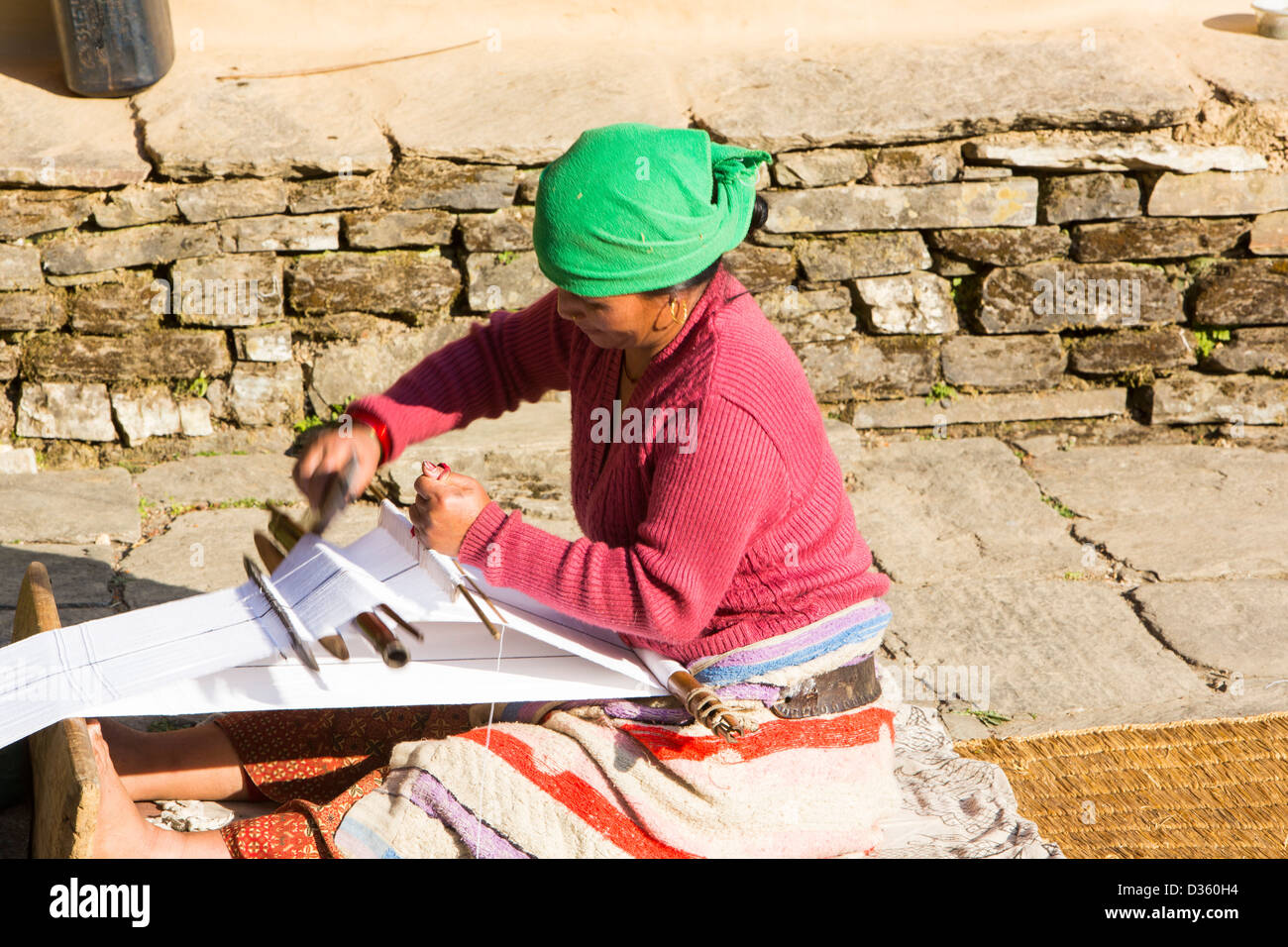 A Nepalese woman in traditional clothing weaving cloth on a hand loom ...