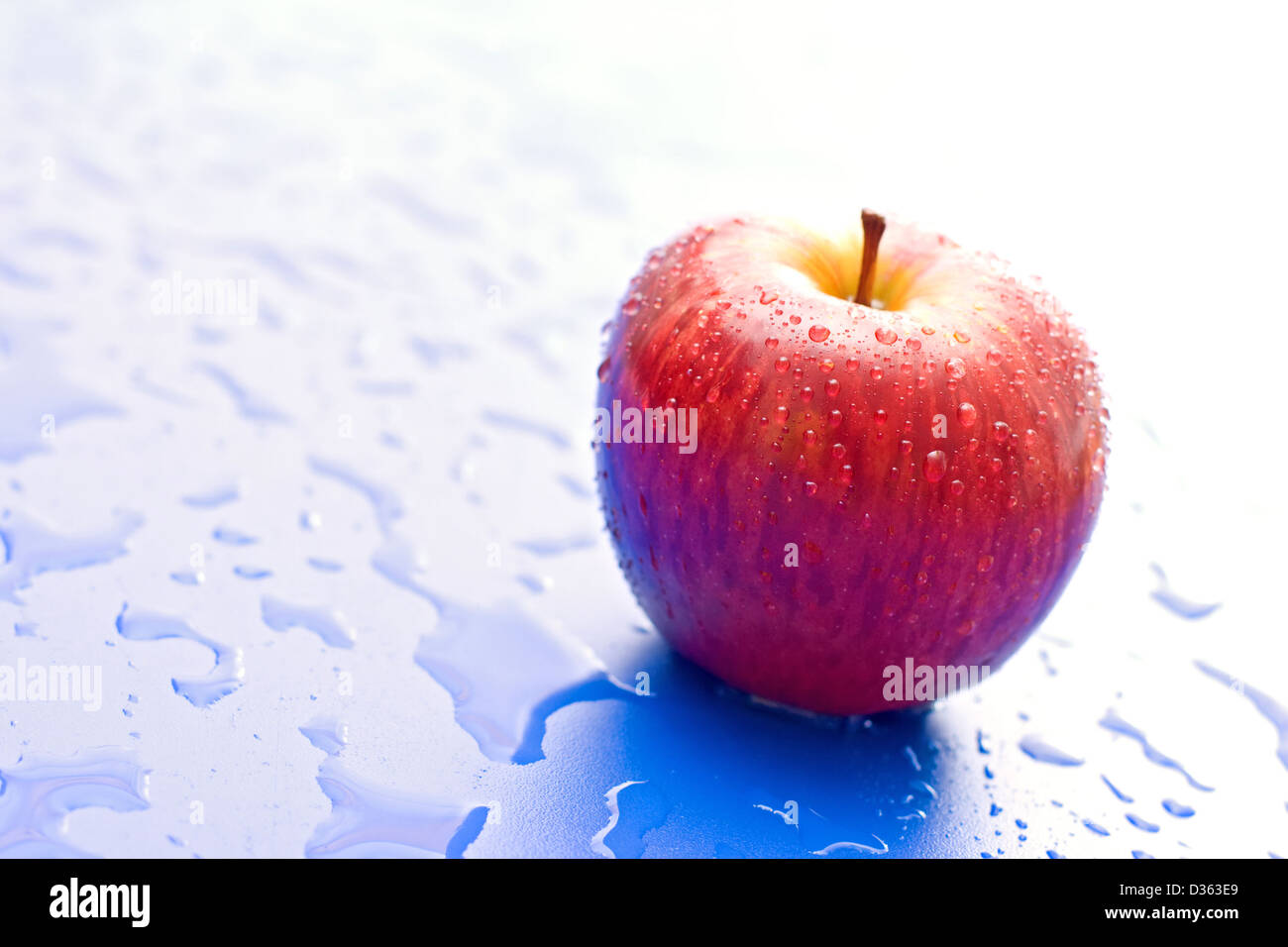 Whole red apple on wet blue surface Stock Photo - Alamy