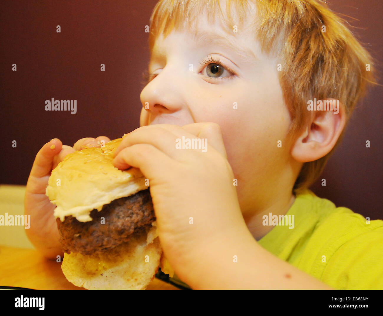 A young boy eats a hamburger with chips and tomato sauce at the table ...