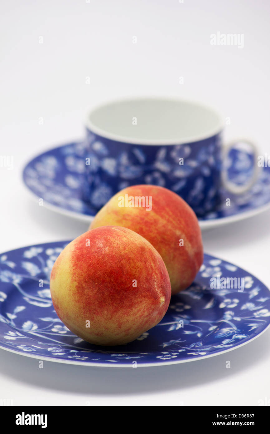 Two peaches on a blue plate on white background Stock Photo - Alamy