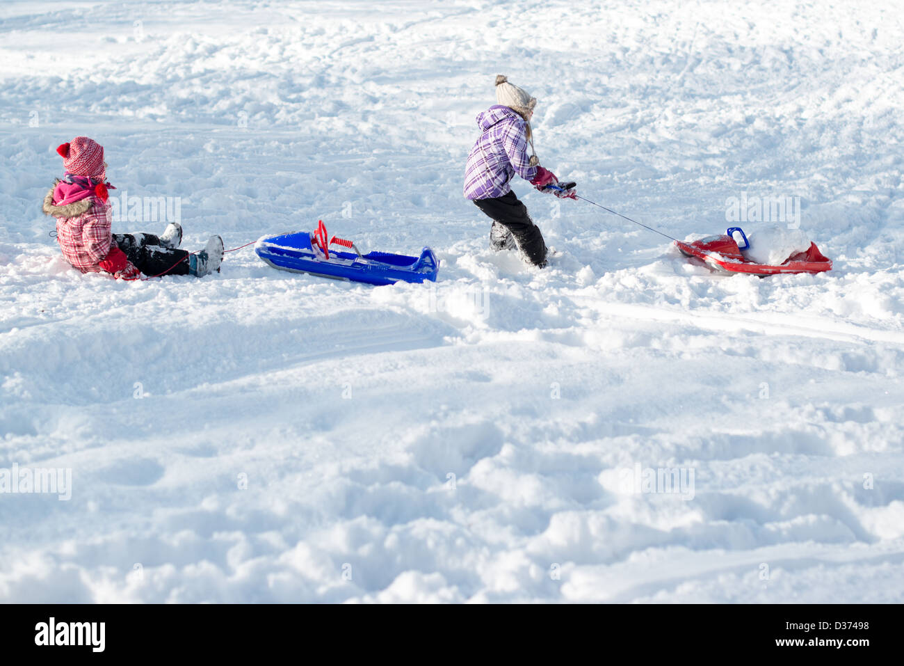 Two kids having fun with their sledges, bright and white winter scene ...