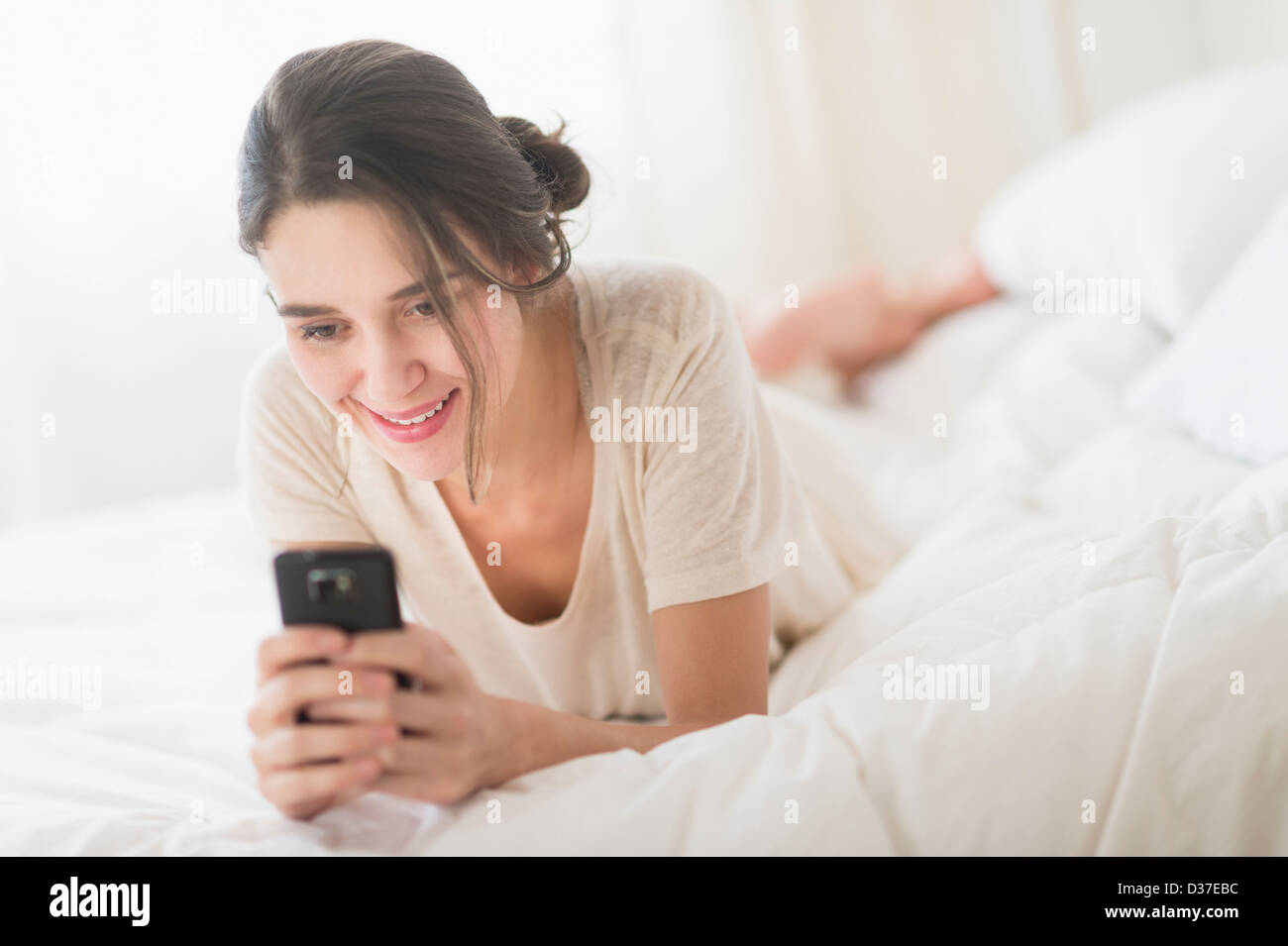 USA, New Jersey, Jersey City, Woman lying in bed and text messaging ...