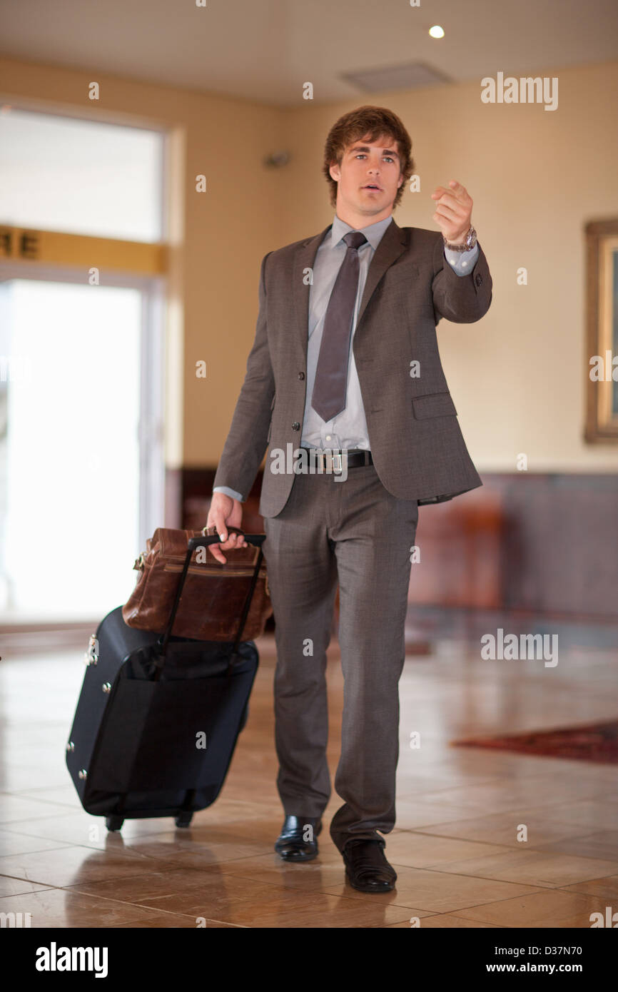 Businessman rolling luggage in lobby Stock Photo - Alamy