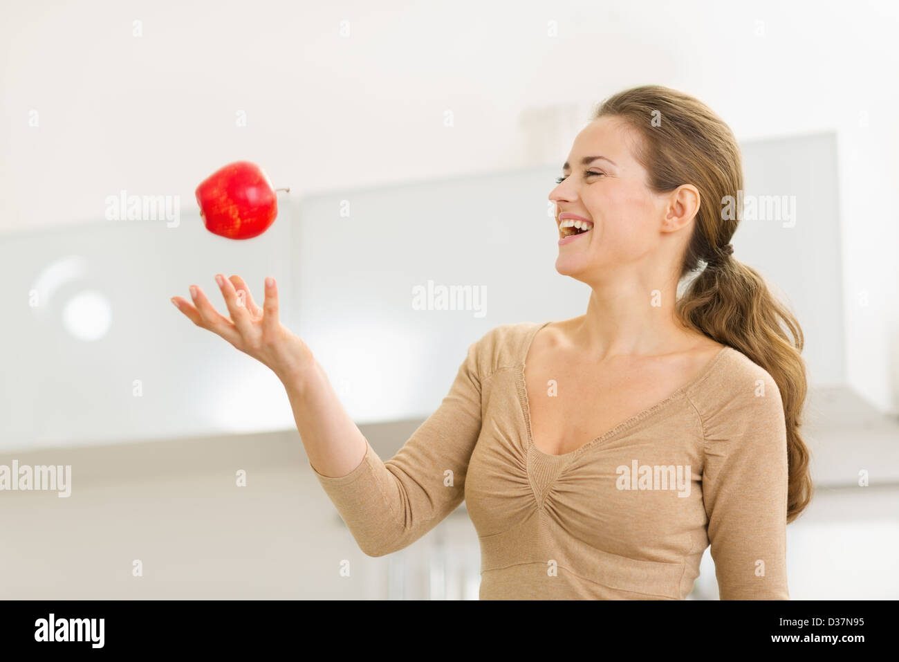 Young woman throwing apple in kitchen Stock Photo - Alamy