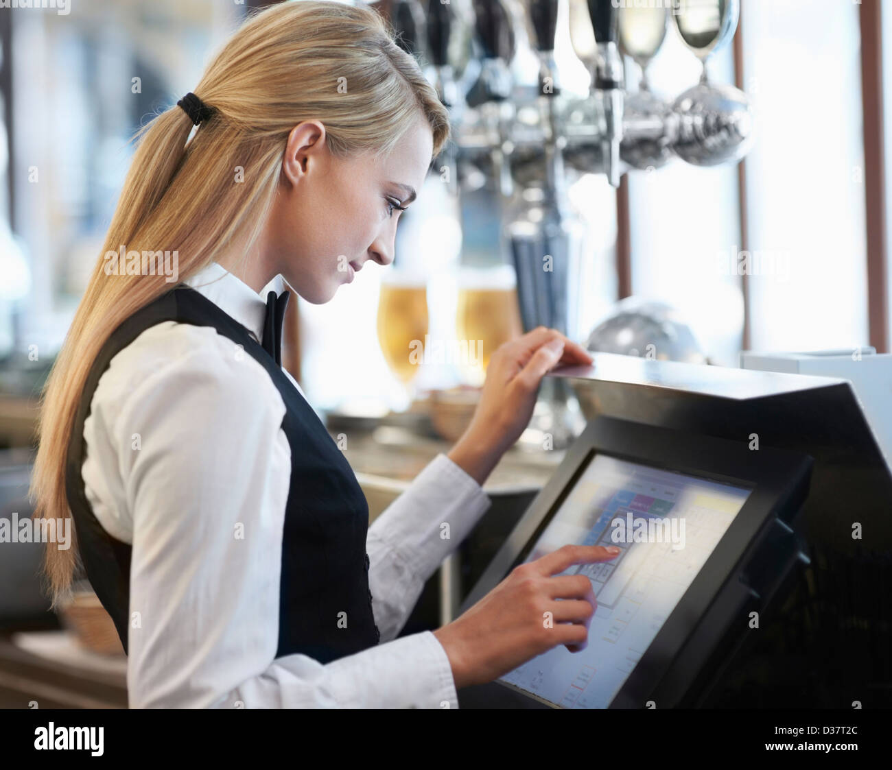 Denmark, Aarhus, Young waitress using computer at restaurant counter ...
