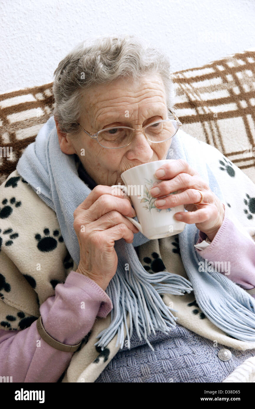 Elderly woman keeping warm in winter wrapped up with blankets & a scarf ...
