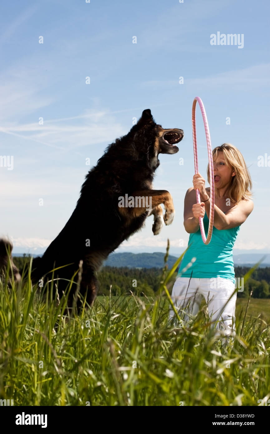 Young woman with jumping dog on a lawn. In the background, mountains ...