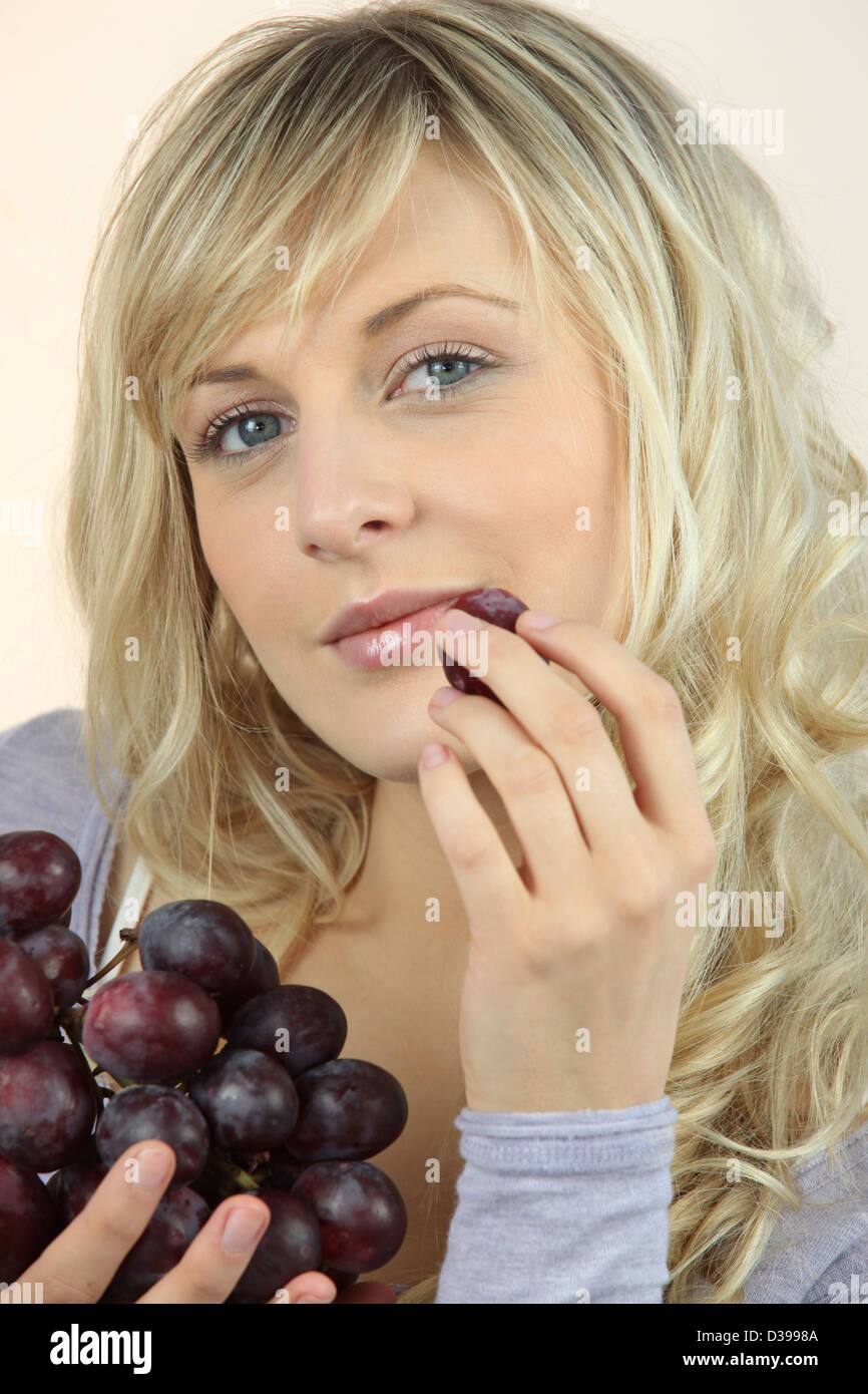 Blond woman about to eat a grape Stock Photo - Alamy
