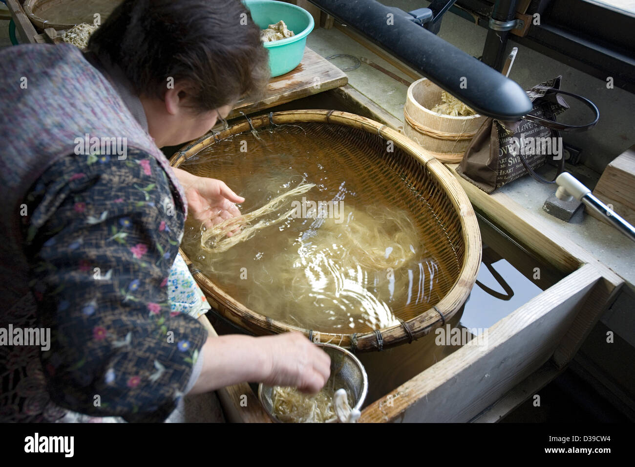 Woman sorting mulberry bark fibers by hand in a sink, called chiritori ...