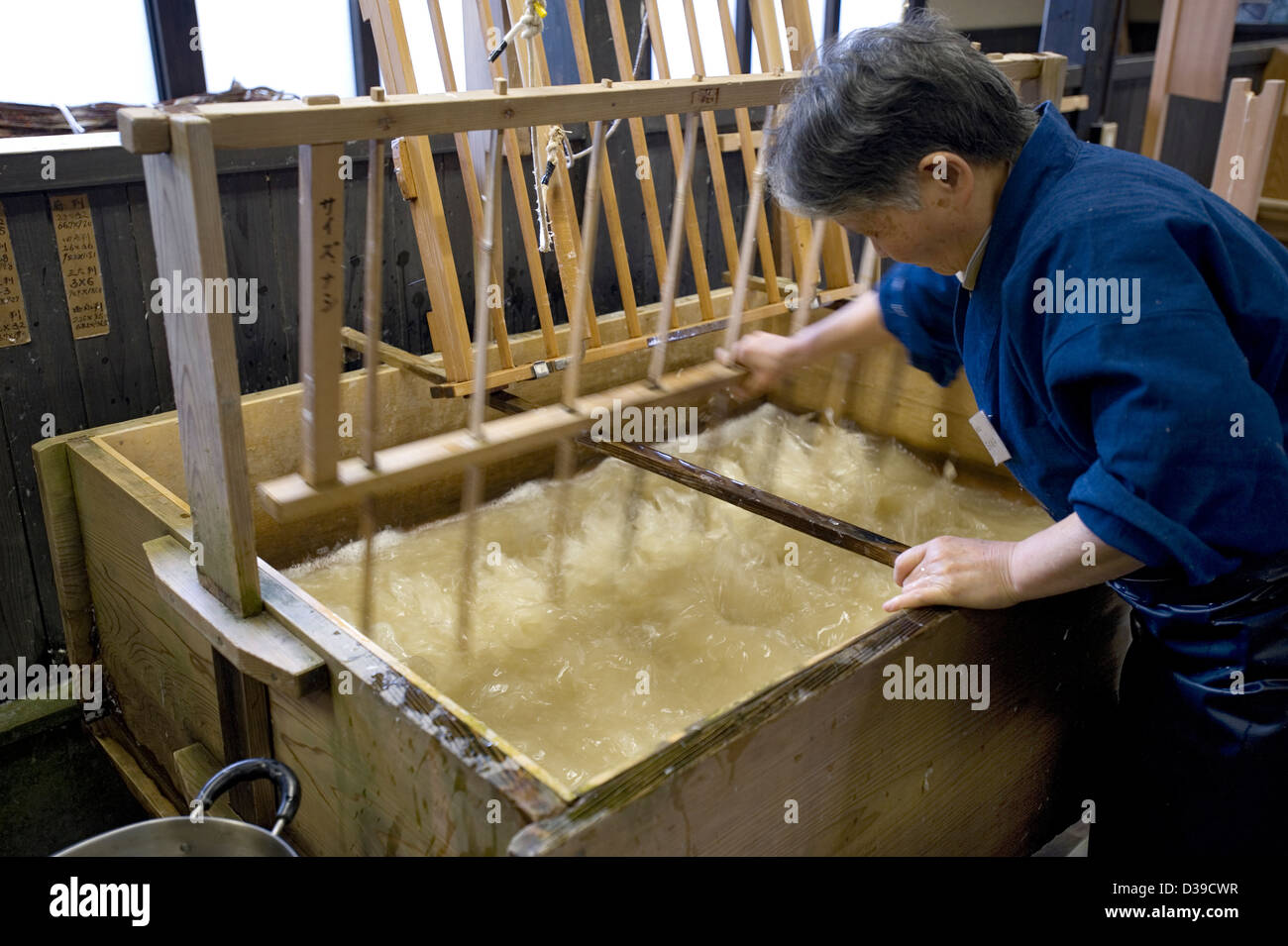 Woman using an umaguwa comb-like tool for mixing water and paper fibers ...