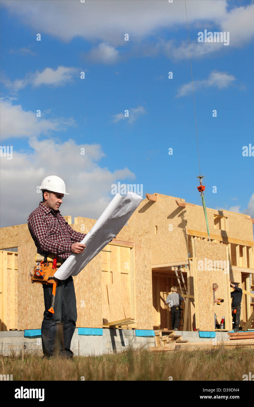 Foreman overlooking construction of wooden house Stock Photo - Alamy