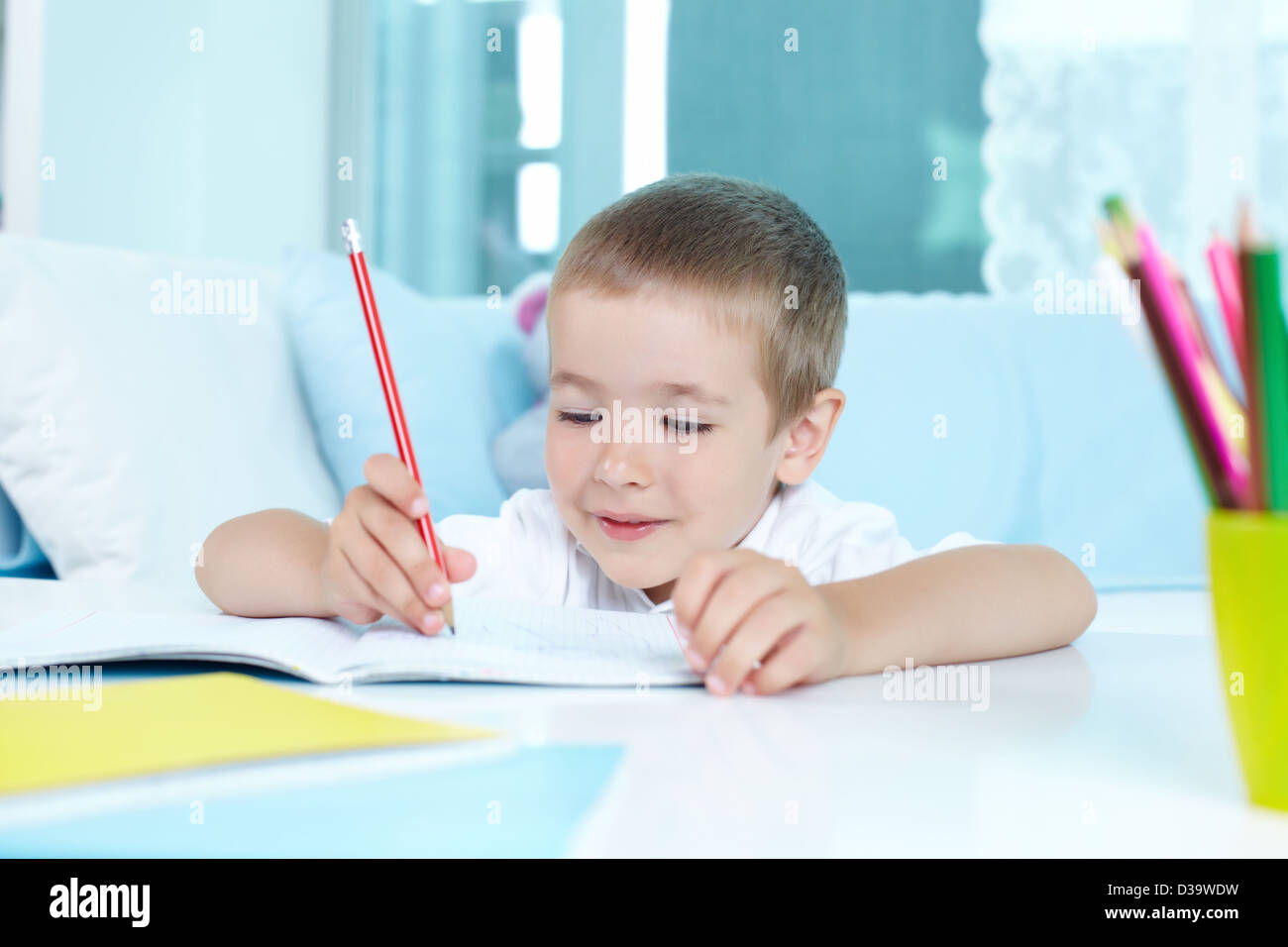 Smiling boy looking at his drawing while sitting by table Stock Photo ...