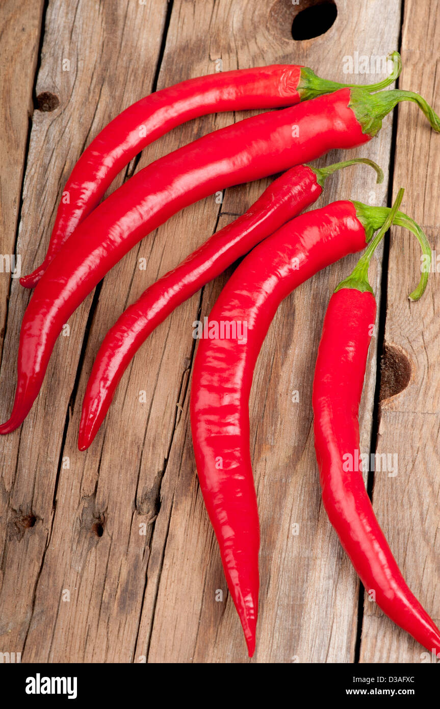 Five vibrant and freshly harvested red chili peppers on an old wooden ...