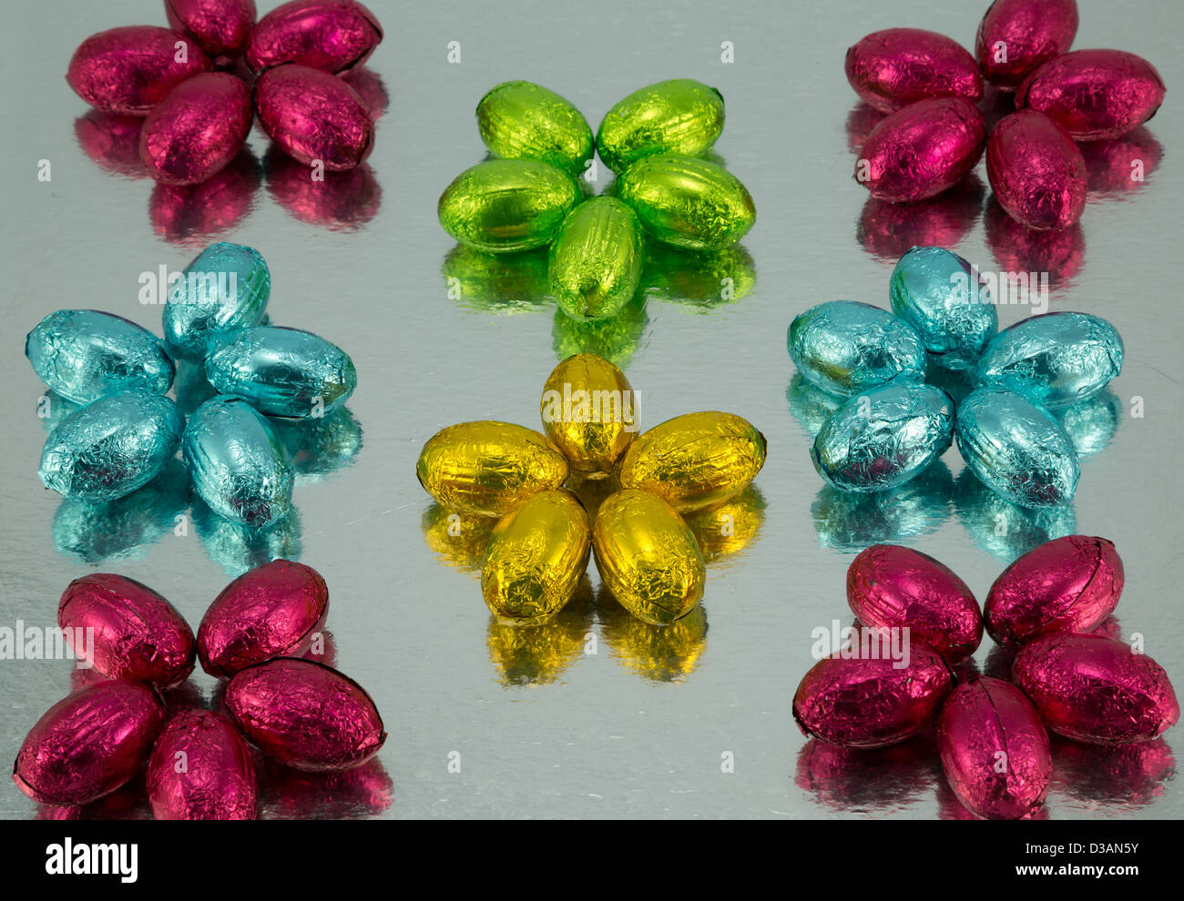 Brightly coloured foil wrapped Easter Eggs arranged in star shapes on a ...