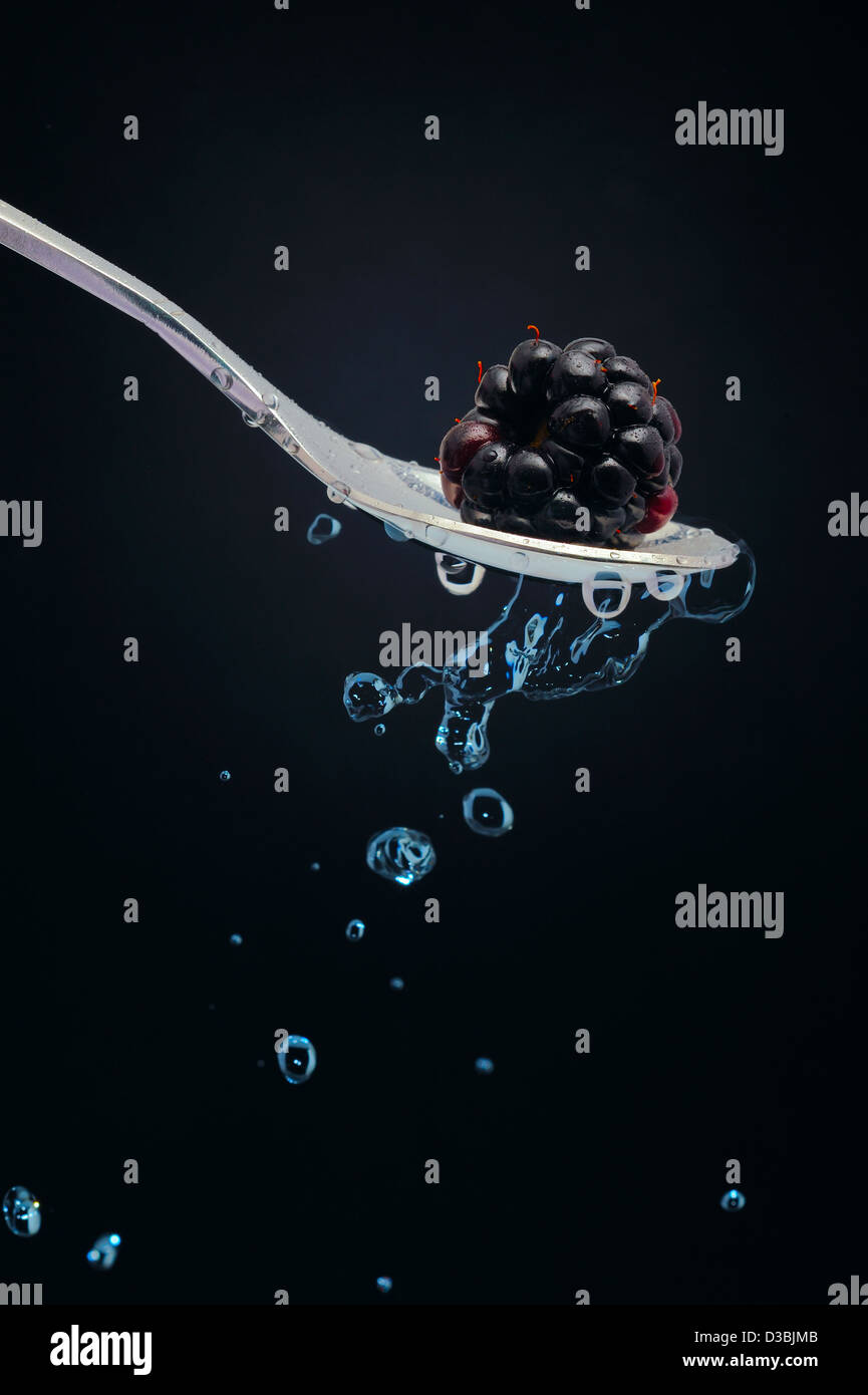 Teaspoon with blackberry and dripping natural mineral water in black ...