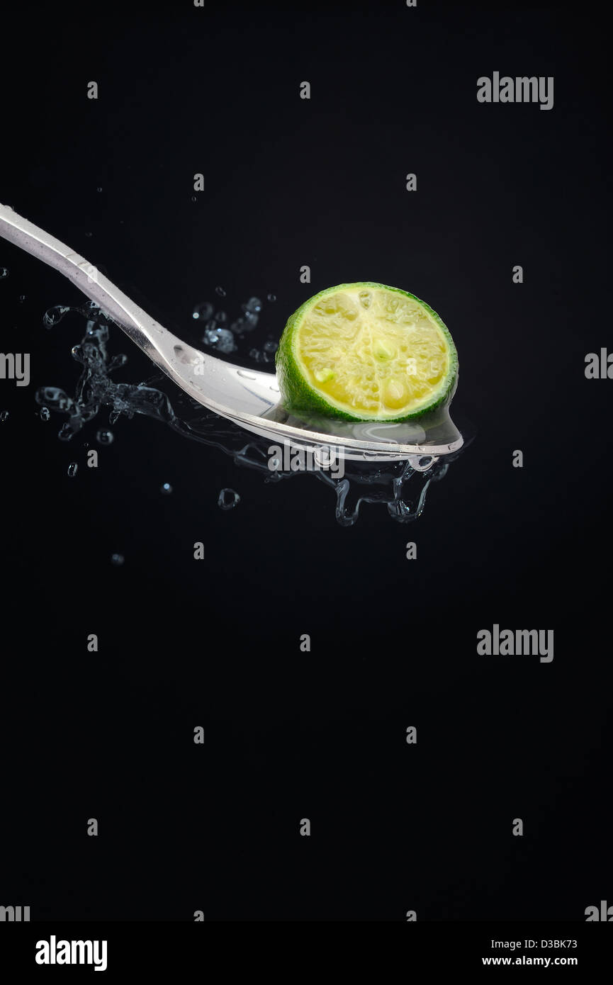 Teaspoon with lime and dripping natural mineral water in black ...