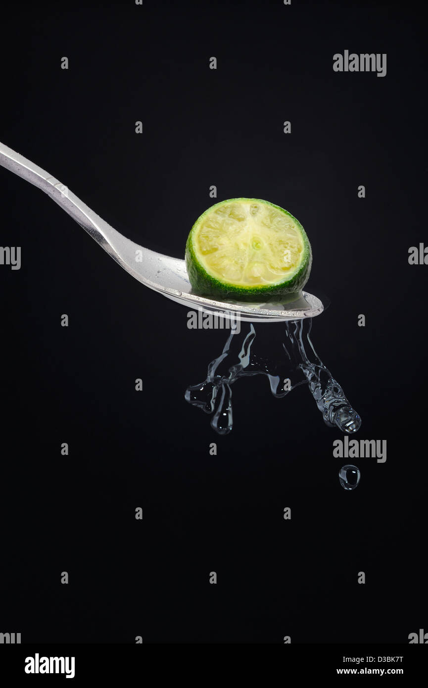 Teaspoon with lime and dripping natural mineral water in black ...