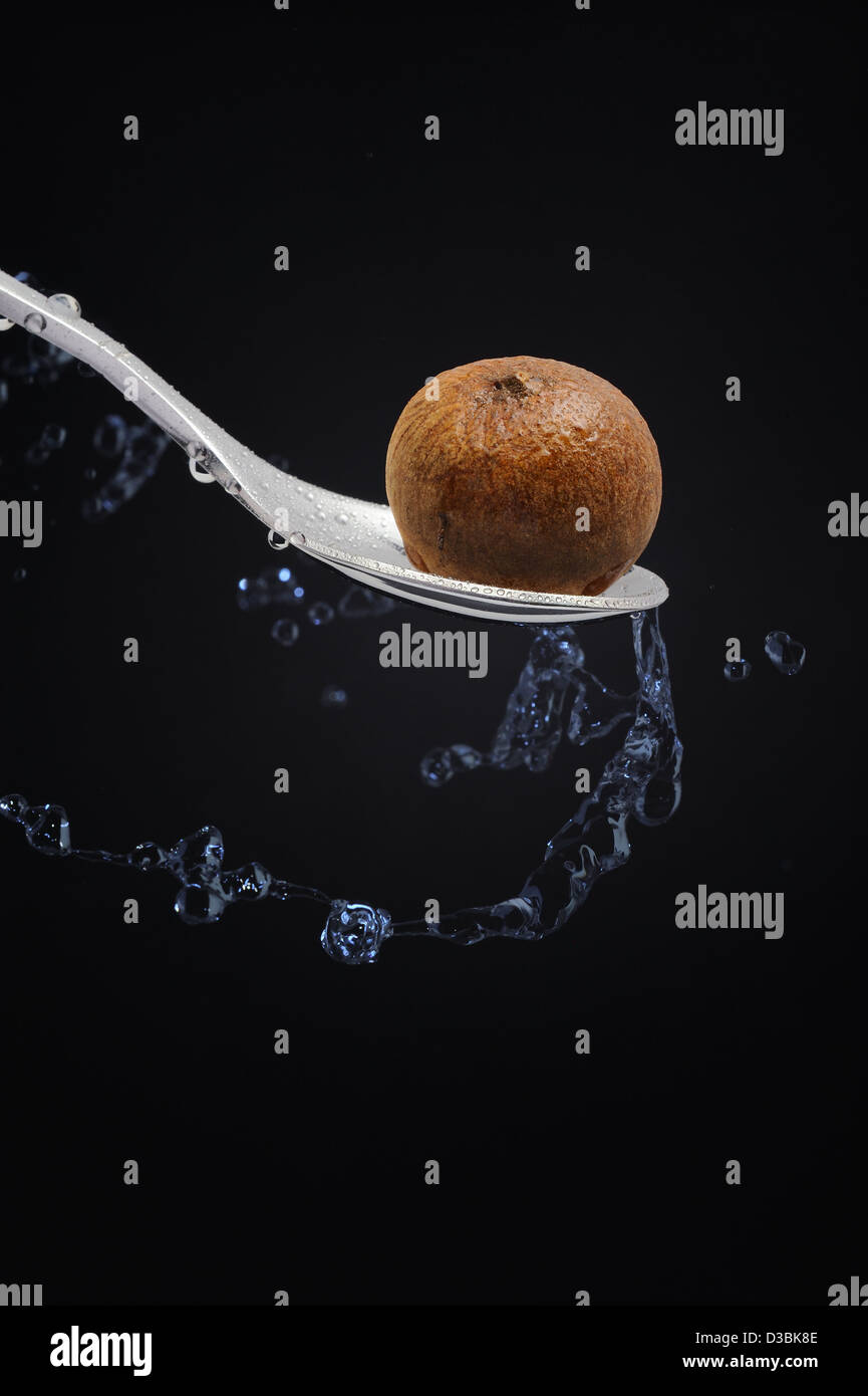 Teaspoon with longan fruit and dripping natural mineral water in black ...